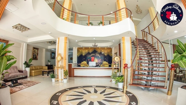 Um hall espaçoso com um design circular no chão, um balcão de recepção e uma imponente escadaria.