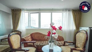 Sala de estar com sofá, duas poltronas, mesa de centro e planta em vaso com flores vermelhas e brancas.