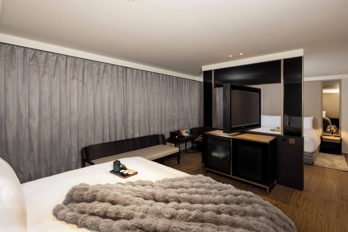 Quarto de hotel moderno com cama, escrivaninha, televisão e área de estar.
