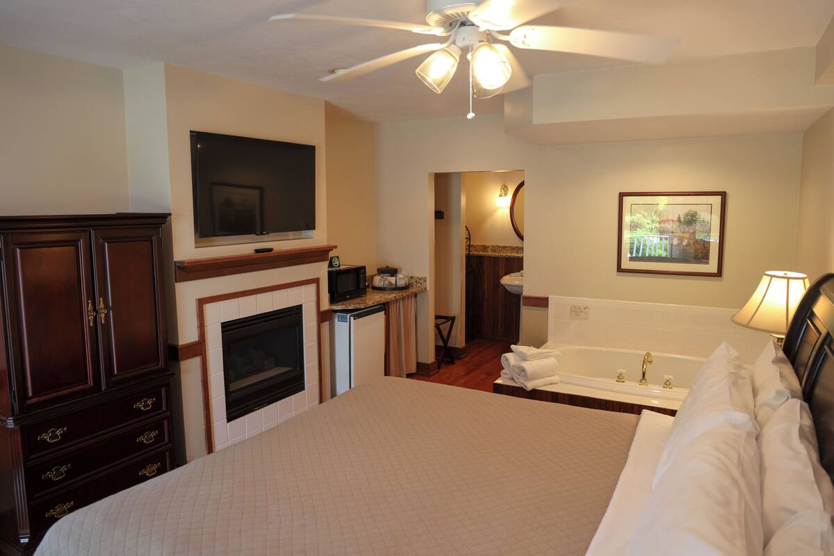 Quarto de hotel com cama, televisão, lareira, banheira e ventoinha de teto.