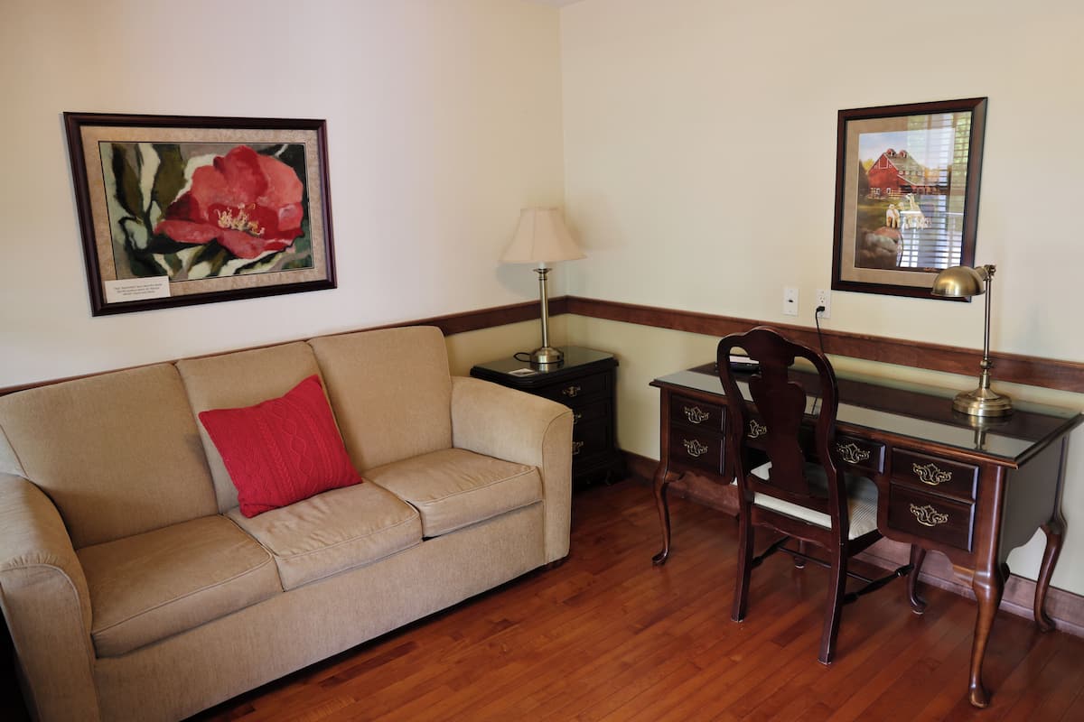 Quarto com sofá bege, escrivaninha de madeira e duas molduras na parede.