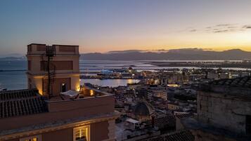 Paisagem urbana costeira ao entardecer, com um edifício de destaque com escadaria em espiral e terraço no telhado.