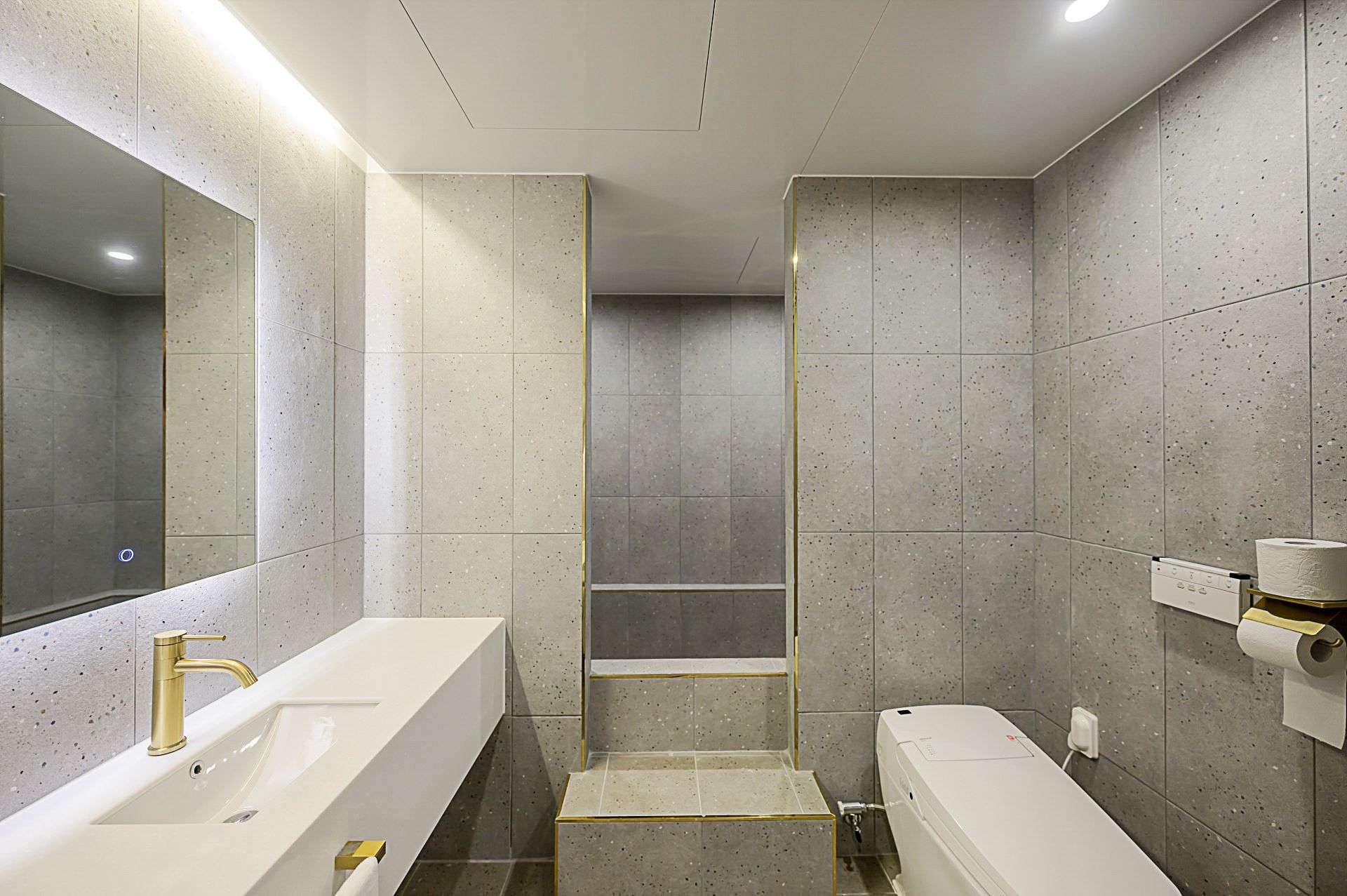 Casa de banho moderna com lavatório branco, torneira dourada e sanita.
