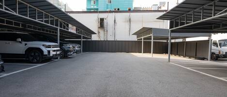 Uma área de estacionamento com vários carros, um edifício com fachada azul e uma galeria coberta.