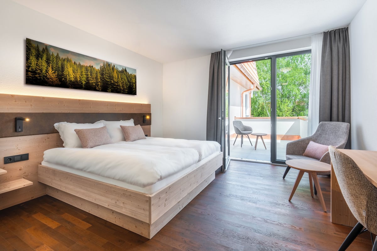 Quarto de hotel moderno com cama de madeira, uma janela grande e vista para o exterior.
