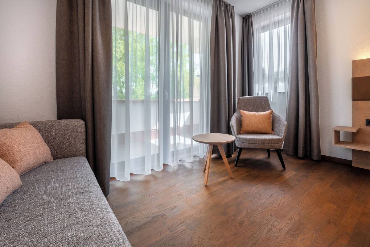 Uma sala de estar moderna com um sofá, uma poltrona, uma mesinha redonda e cortinas leves.