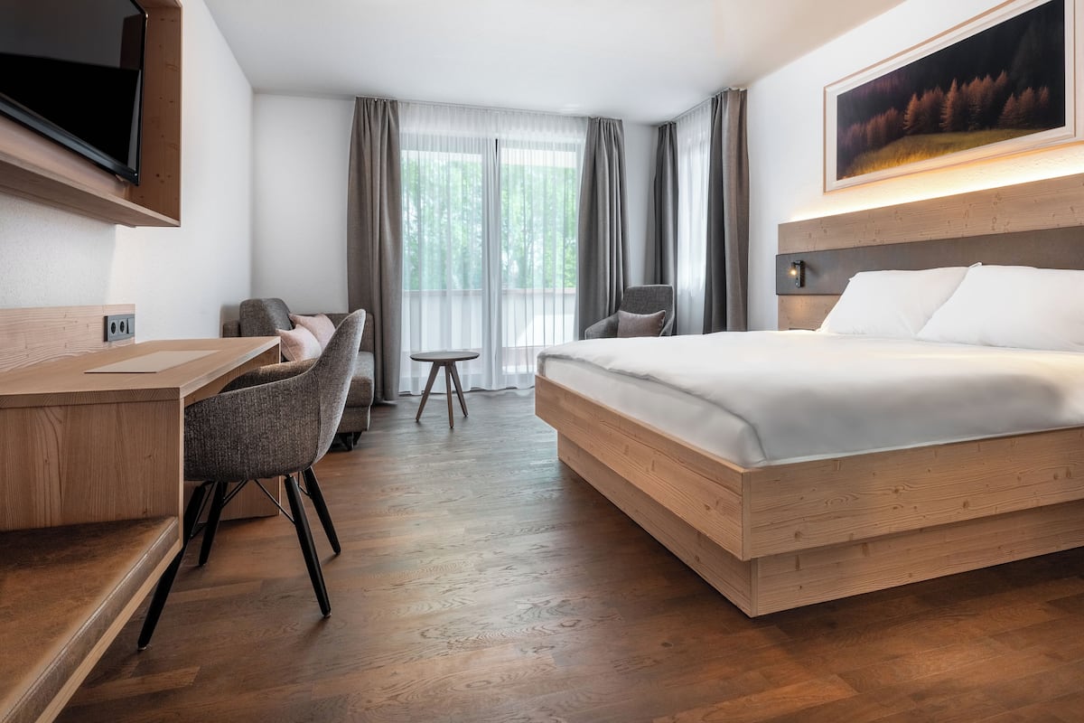 Quarto de hotel moderno com cama de madeira, escrivaninha, cadeira e TV fixada na parede.
