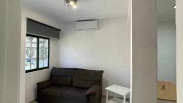 Uma sala de estar moderna com um sofá marrom escuro, uma mesa pequena branca e um lustre.