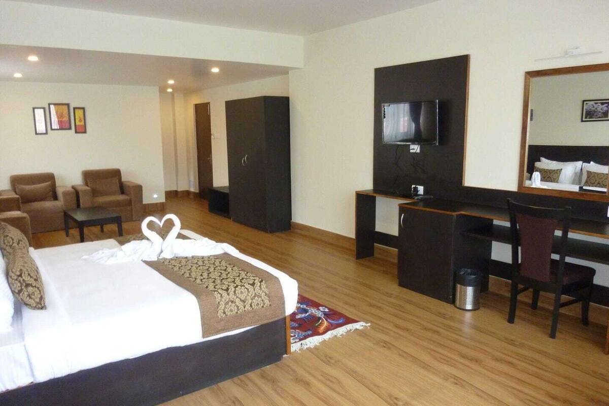 Quarto de hotel com uma cama, duas poltronas, uma mesa de trabalho, uma televisão e um espelho.