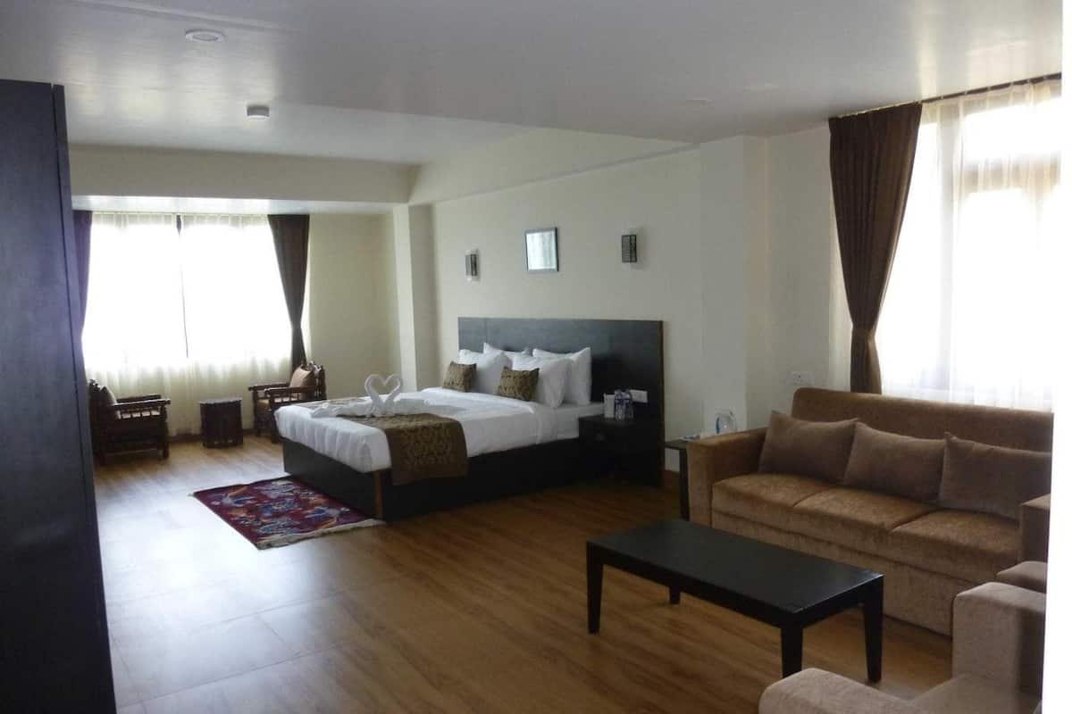 Quarto de hotel com cama, sofá, mesa de centro e pequena mesa com abajur.