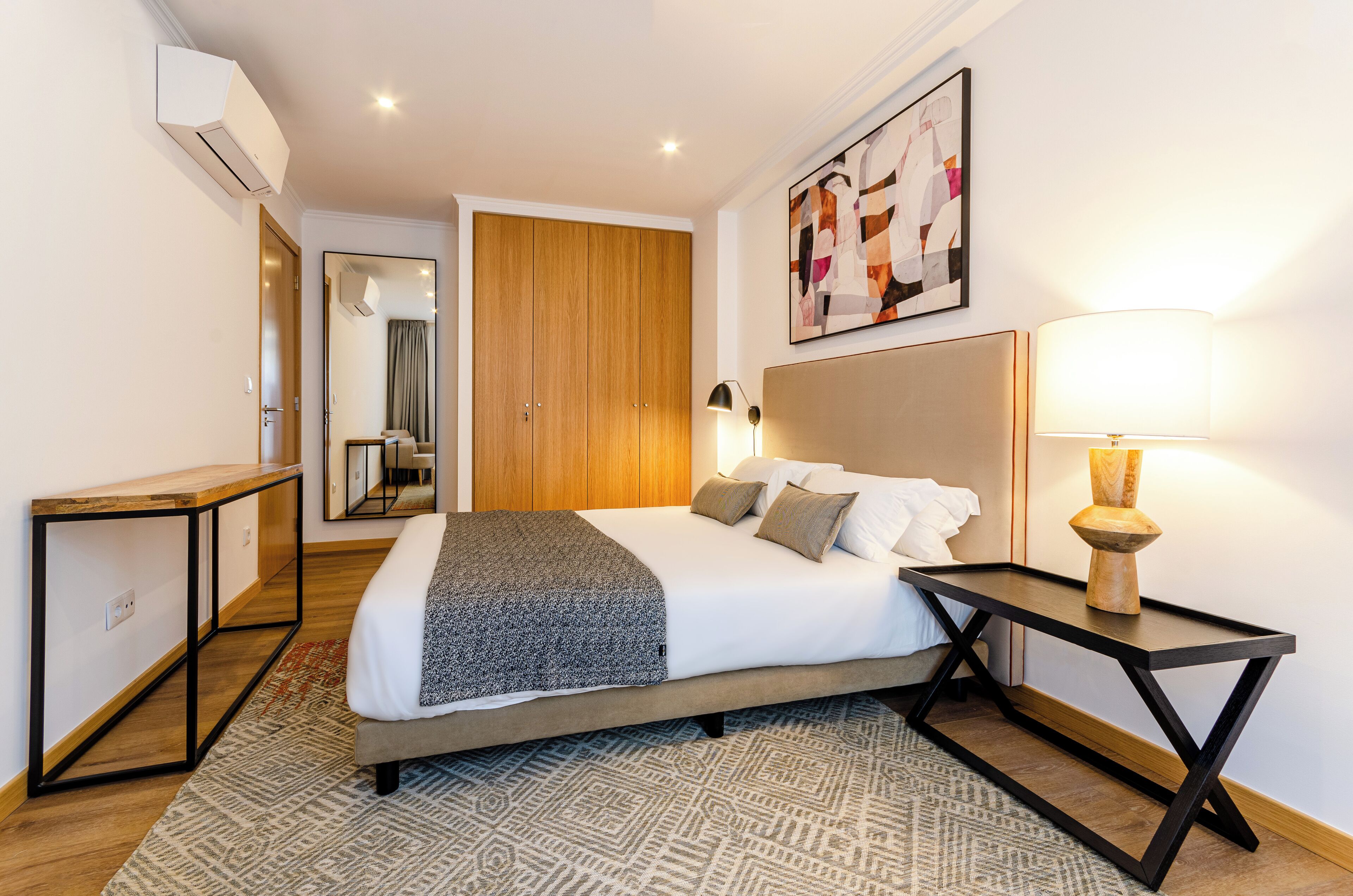 Quarto de hotel com cama, mesa de cabeceira, abajur e espelho.