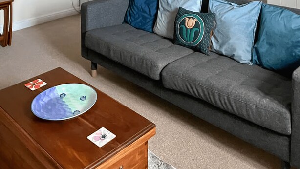 Sala de estar com sofá cinza, almofadas azuis e verde-água, mesa de centro de madeira com cartas de baralho e radiador branco.