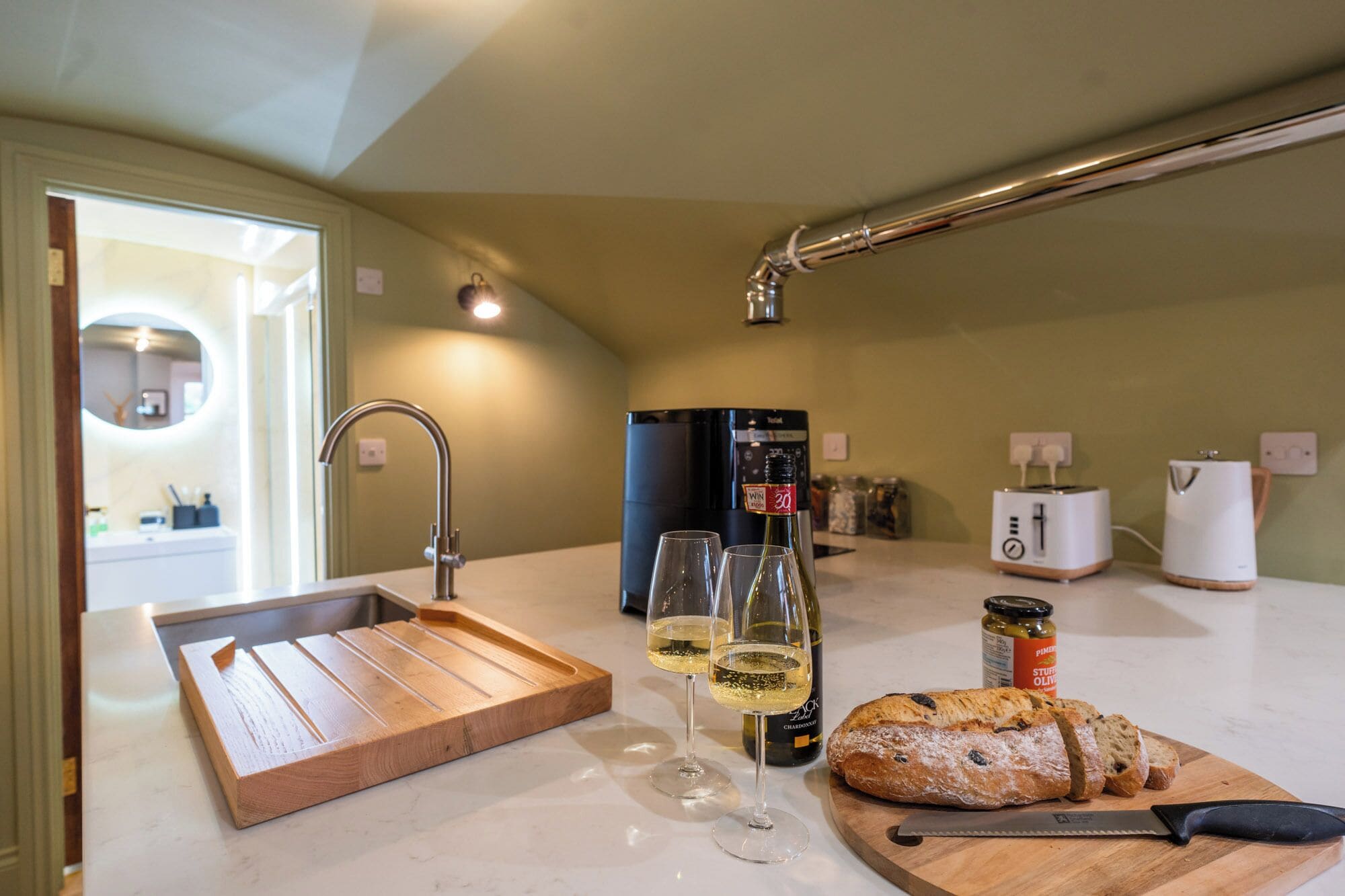 Cozinha com pia, cafeteira, torradeira, pão e duas taças de vinho branco no balcão.