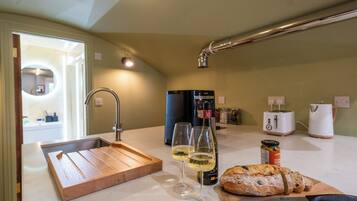 Cozinha com pia, cafeteira, torradeira, pão e duas taças de vinho branco no balcão.