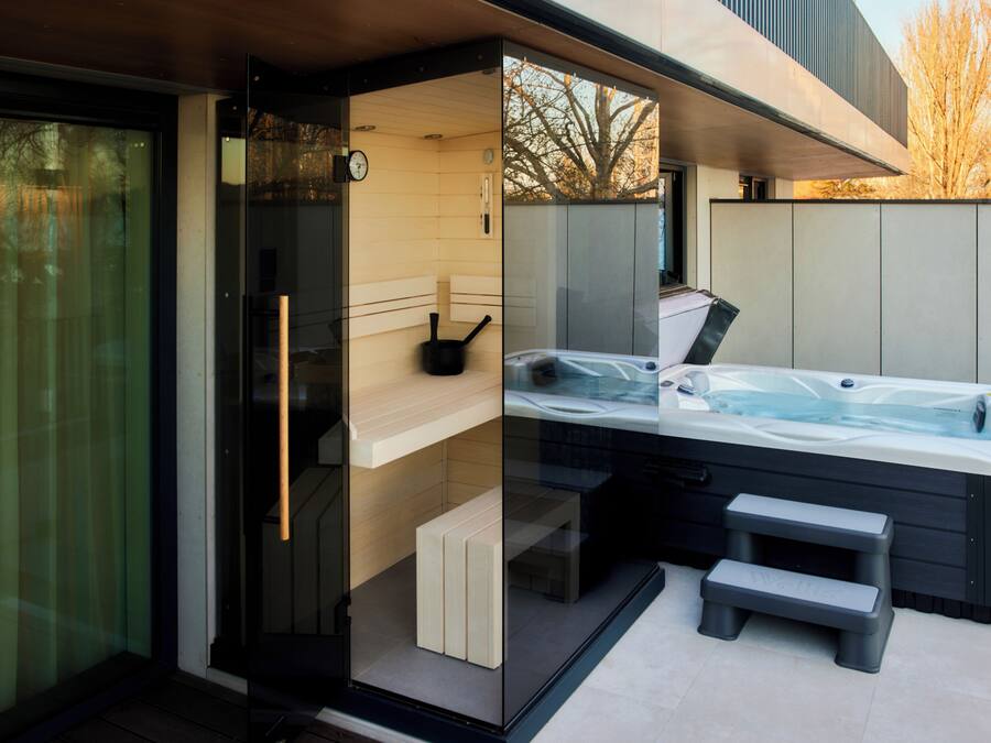 Uma área de spa moderna com sauna envidraçada, hidromassagem e um banco de madeira.