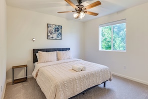Quarto com uma cama, um ventilador de teto, uma janela e um quadro na parede.