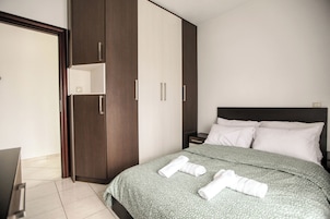 Quarto de hotel com cama, guarda-roupa e mesa de cabeceira.