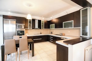 Uma cozinha moderna com armários escuros, uma geladeira de aço inoxidável, micro-ondas e uma área de jantar com mesa e cadeiras.