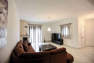 Uma sala de estar moderna com um sofá marrom, televisão de tela plana, lareira e um espaço de jantar com mesa de centro.