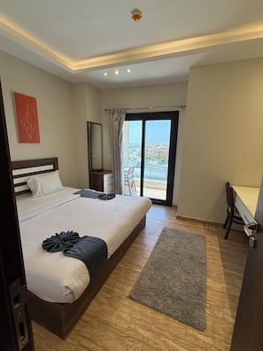 Quarto de hotel com cama, escrivaninha, cadeira, vista pela janela e iluminação no teto.