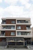 Um edifício moderno de vários andares, com varandas em cada pavimento e entrada protegida por portão.