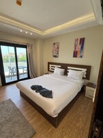 Quarto de hotel com uma cama grande, mesa de cabeceira, cortinas e uma obra de arte na parede.
