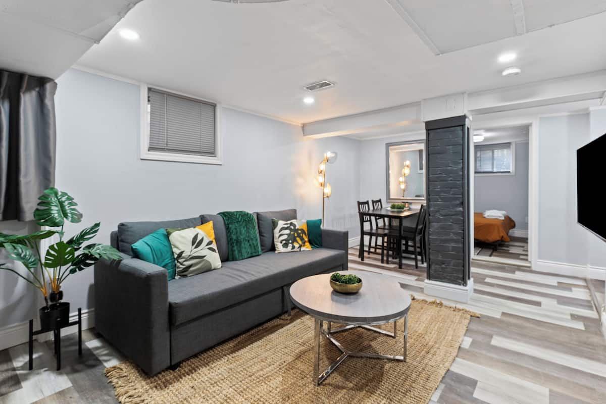 Uma sala de estar moderna com um sofá cinzento, uma mesa de centro redonda e uma área de jantar com mesa e cadeiras.