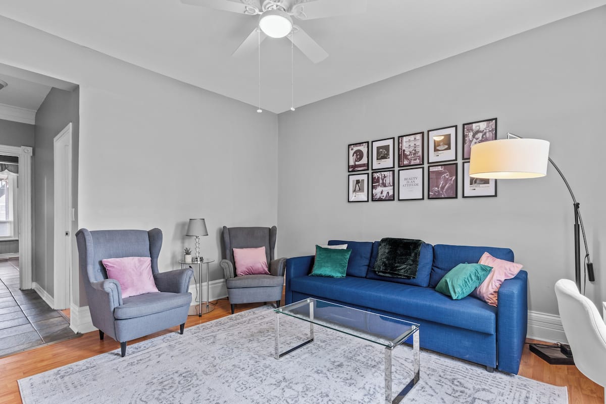 Uma sala de estar moderna com uma poltrona cinza, um sofá azul e uma mesa de centro de vidro.