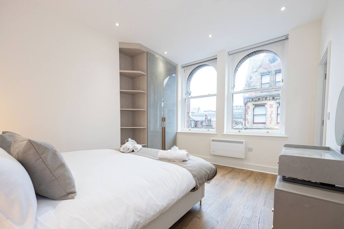 Quarto moderno com cama grande, estantes embutidas e janelas amplas com arcos.