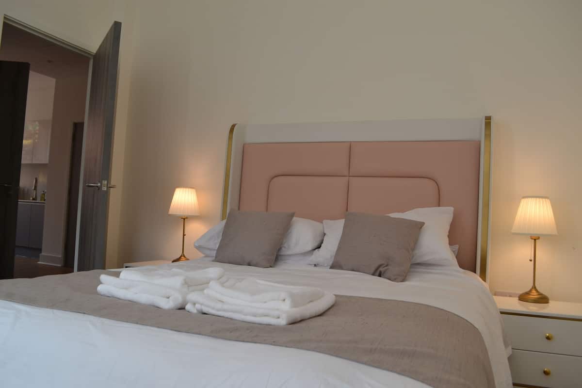 Cama bem arrumada com toalhas dobradas, cabeceira, abajures e mesa de cabeceira.