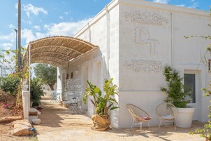 Um edifício branco com alpendre coberto, mesas ao ar livre e plantas em vasos.