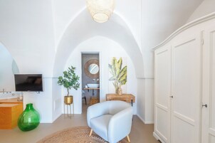 Um interior moderno com uma televisão, um vaso verde, uma poltrona azul clara e um guarda-roupa branco grande.