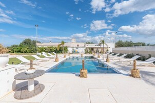 Uma área de piscina com espreguiçadeiras e uma mesa de madeira, cercada por uma grade e vegetação.