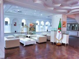 Um amplo hall de hotel com design moderno, apresentando uma área de estar central com sofás e uma exposição de bandeiras.