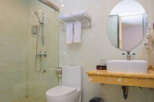 Casa de banho com chuveiro em cabine de vidro, sanita, lavatório com espelho e suporte para toalhas.