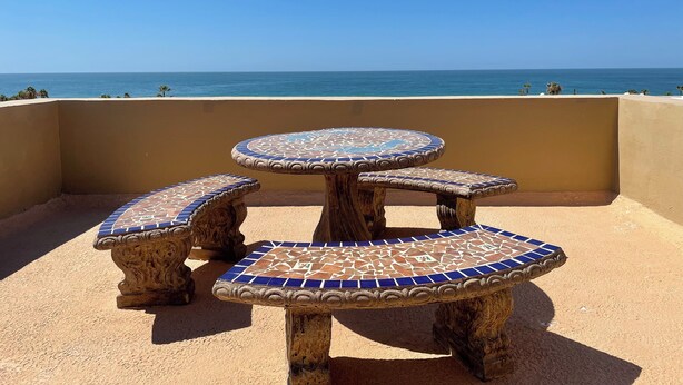 Mesa redonda com assentos de mosaico em varanda com vista para o mar.