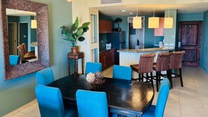Uma área de refeições com uma mesa de madeira escura e cadeiras azuis, um espelho grande e um vaso com planta.