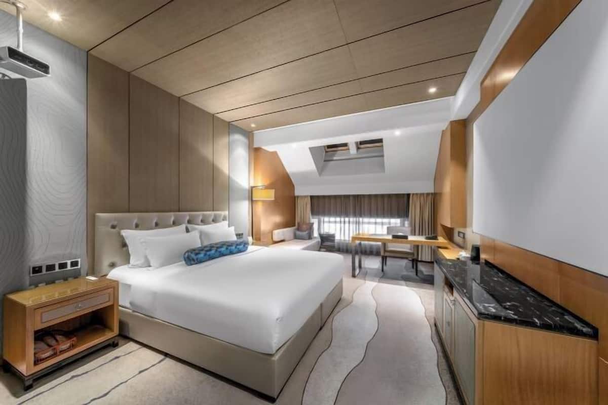 Quarto de hotel moderno com uma cama grande, uma mesa de escritório e uma cozinha compacta.