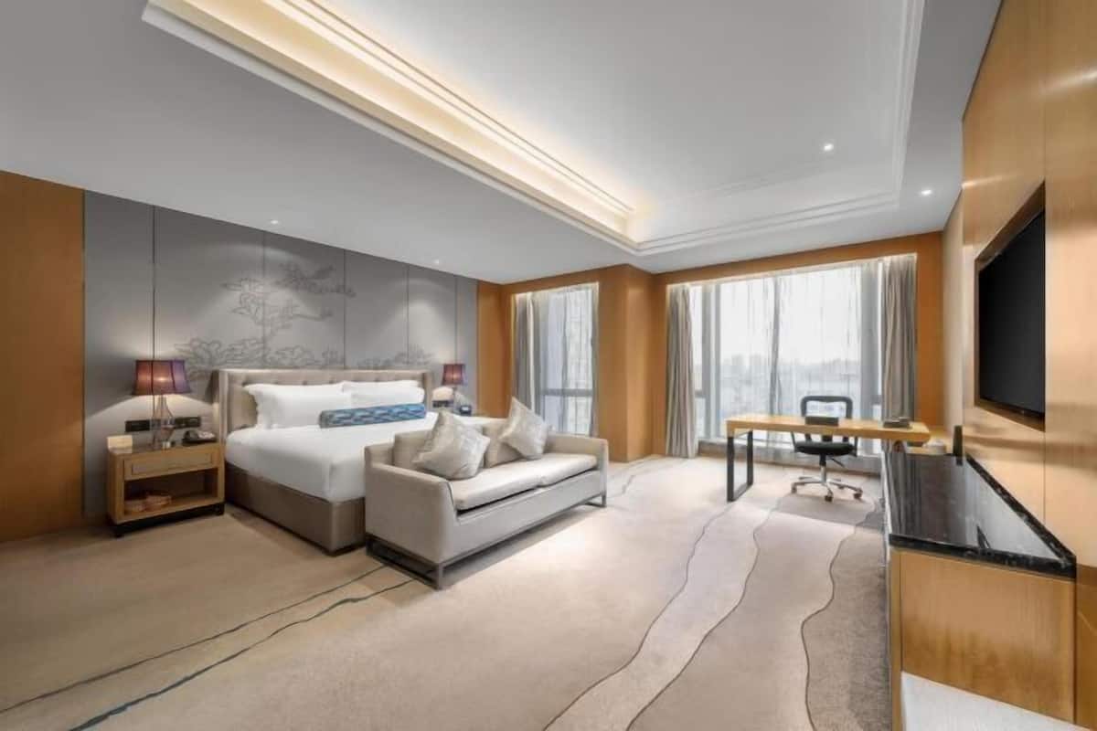 Quarto de hotel moderno com cama, sofá, escrivaninha e televisão.