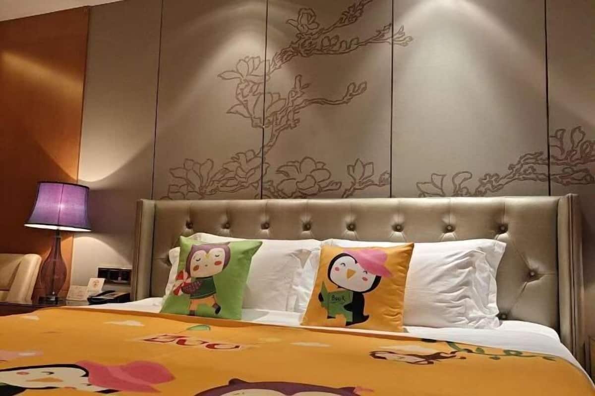 Quarto de hotel com cabeceira estofada, cama com roupa de cama colorida e painel decorativo na parede.