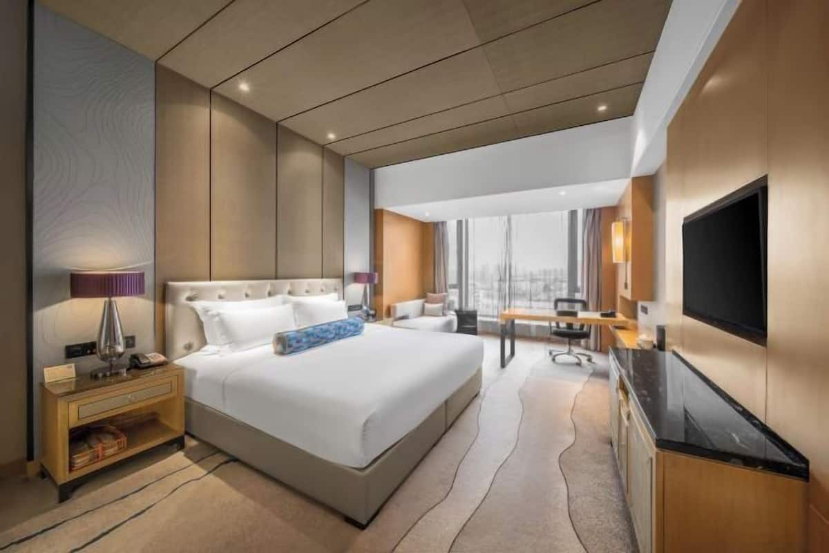 Quarto de hotel moderno com uma cama grande, uma escrivaninha, uma televisão e vista para a cidade.