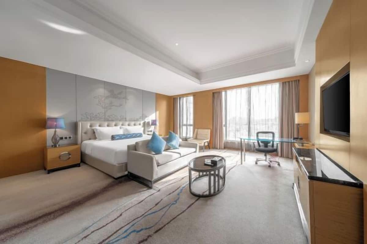 Quarto de hotel moderno com uma cama grande, uma escrivaninha, uma cadeira e uma televisão.