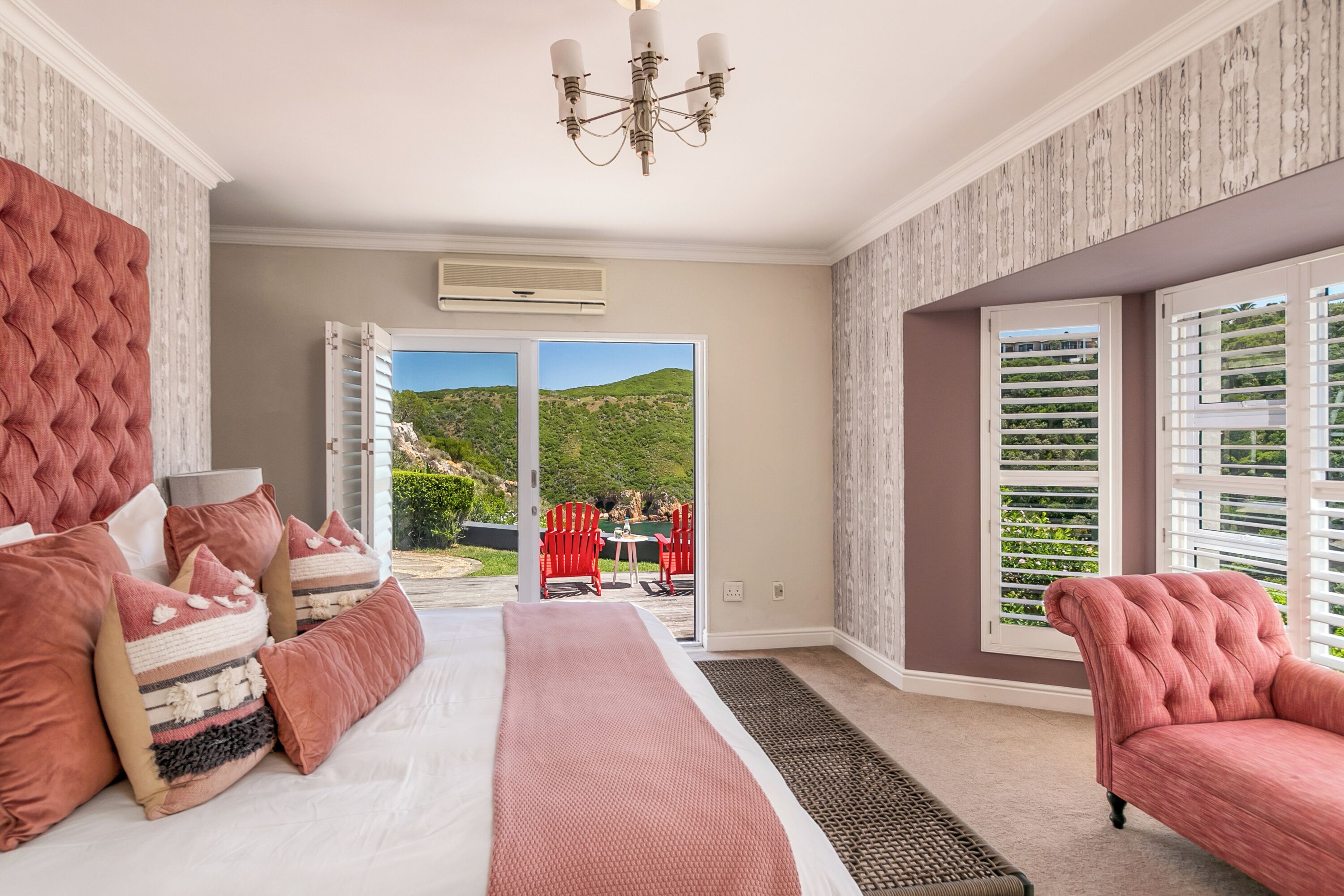 Quarto com uma cama grande, um candelabro e vista para uma paisagem verde pela janela.