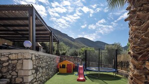 Uma área de recreação infantil com escorrega, trampolim e uma casinha.