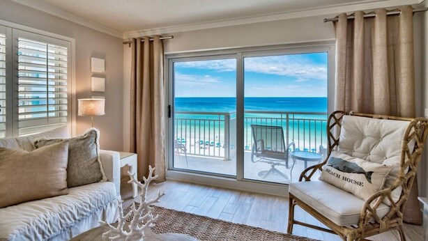Quarto com vista para o oceano, um sofá branco, uma cadeira de vime e uma varanda com mobiliário exterior.
