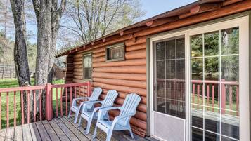 Uma cabana de toras com um alpendre, duas cadeiras Adirondack e uma janela grande.
