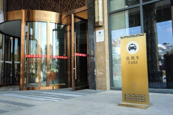 Entrada de hotel com portas giratórias e um aviso indicando ponto de táxi.