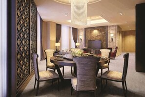 Um salão de refeições de hotel com uma mesa redonda, cadeiras, um candelabro e uma televisão.