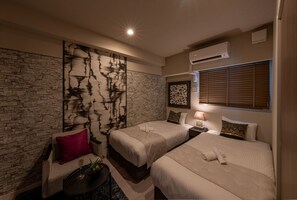 Quarto de hotel com duas camas, uma parede de destaque em pedra, ar condicionado moderno e uma janela com persianas.