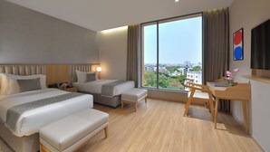 Quarto de hotel moderno com duas camas, uma escrivaninha e uma grande janela com vista para a cidade.